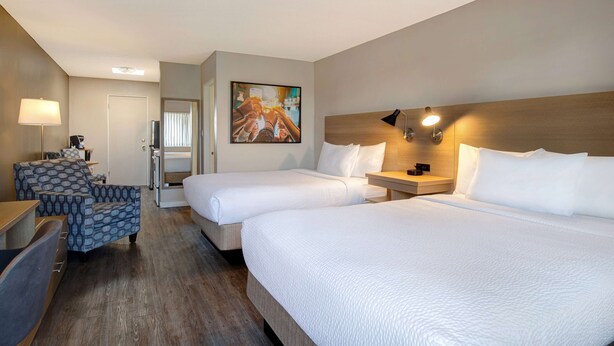 Quarto de hotel com duas camas, um sofá, uma escrivaninha e um quadro na parede.