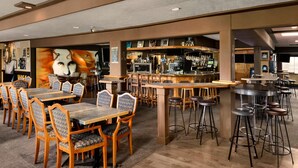 Restaurante com várias mesas e cadeiras, um espaço de bar com banquetas e um mural na parede.