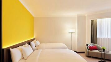 Quarto de hotel com duas camas, um sofá, uma luminária e uma pequena mesa com um vaso.