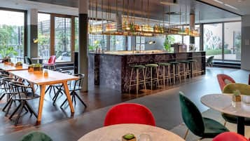 Uma área de bar moderna, com balcão de mármore, banquetas e vista para o verde lá fora.