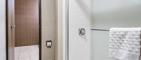 Um banheiro moderno com box de vidro, uma toalha branca pendurada na parede e uma porta que dá para outro cômodo.