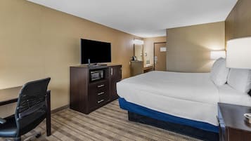 Quarto de hotel com cama, escrivaninha, cadeira, televisão e espelho.