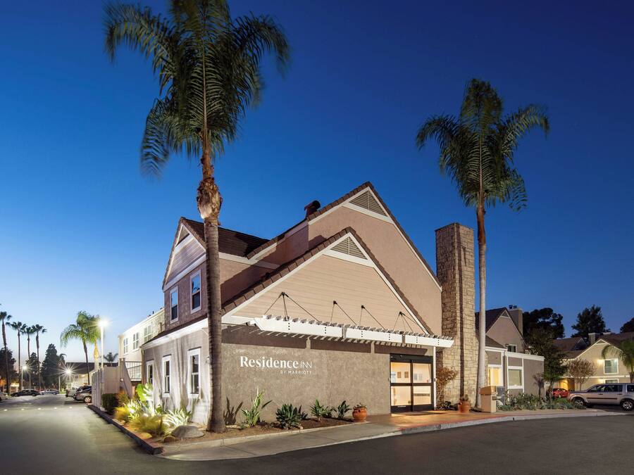 Hotel de dois andares com design moderno, destacando uma entrada imponente e uma área externa coberta.