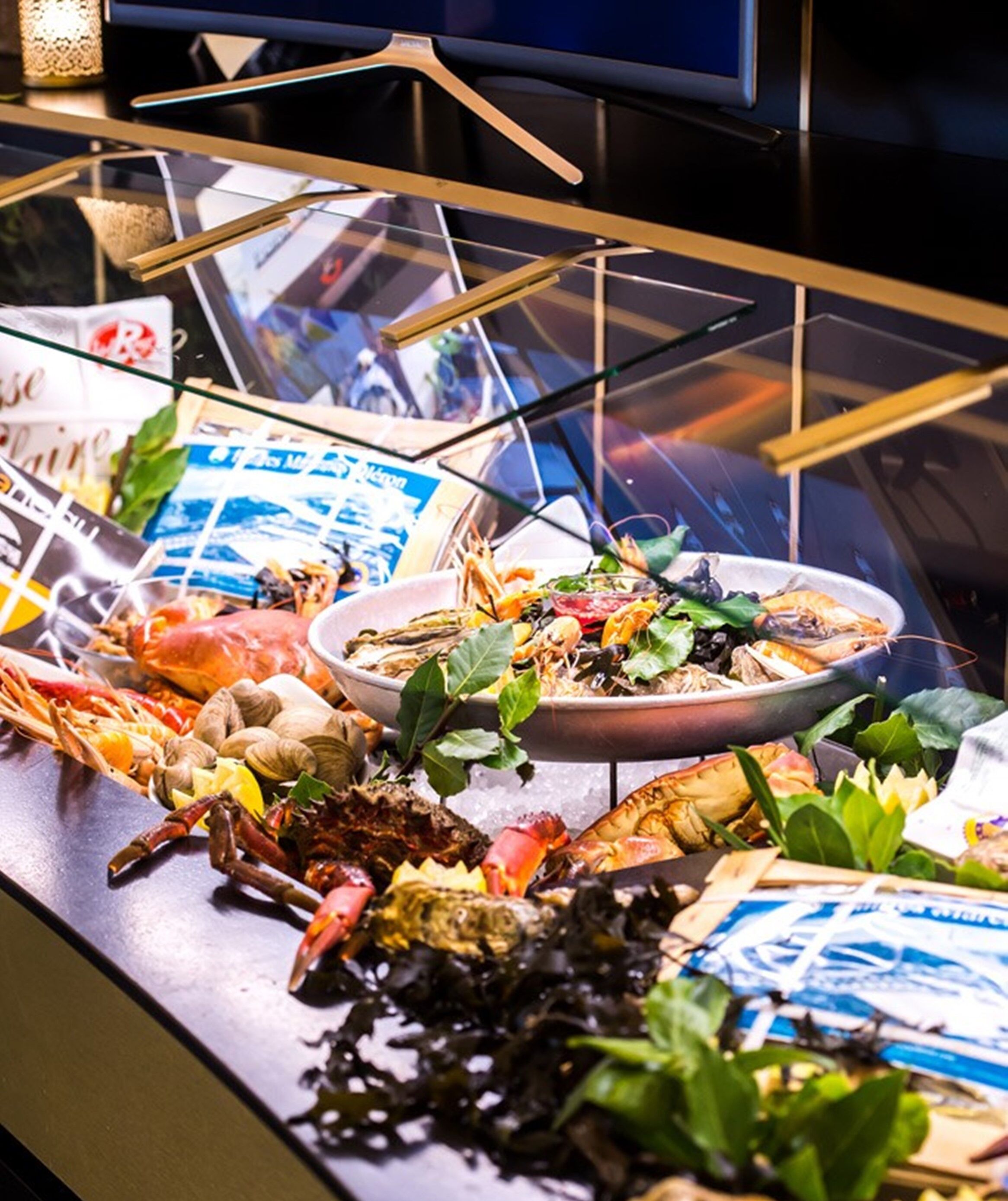 Exposição de frutos do mar com diversos tipos de mariscos e algas marinhas, acompanhada de menus impressos.