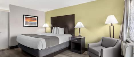 Quarto de hotel com cama, duas luminárias de cabeceira, uma poltrona, mesa de cabeceira e um quadro na parede.