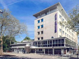 Um hotel moderno com um letreiro chamativo do 'Mercure Hotel', uma entrada coberta e fachada de vidro.