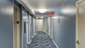 Corredor de hotel com carpete estampado, portas e sinalização de saída.