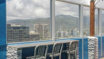 Uma varanda com duas cadeiras, uma mesa e vista para a cidade e montanhas.