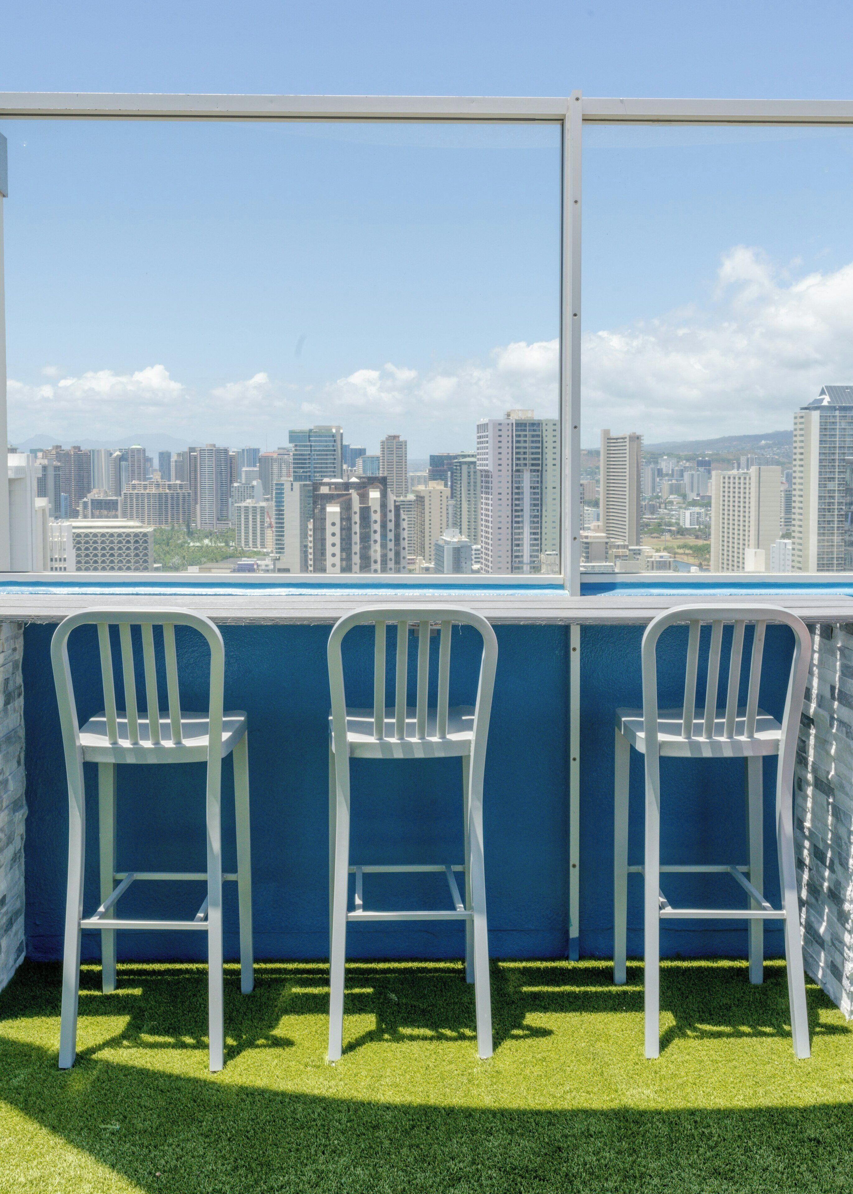 Varanda com três cadeiras de plástico branco e vista para a paisagem urbana.