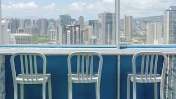 Varanda com três cadeiras de plástico branco e vista para a paisagem urbana.