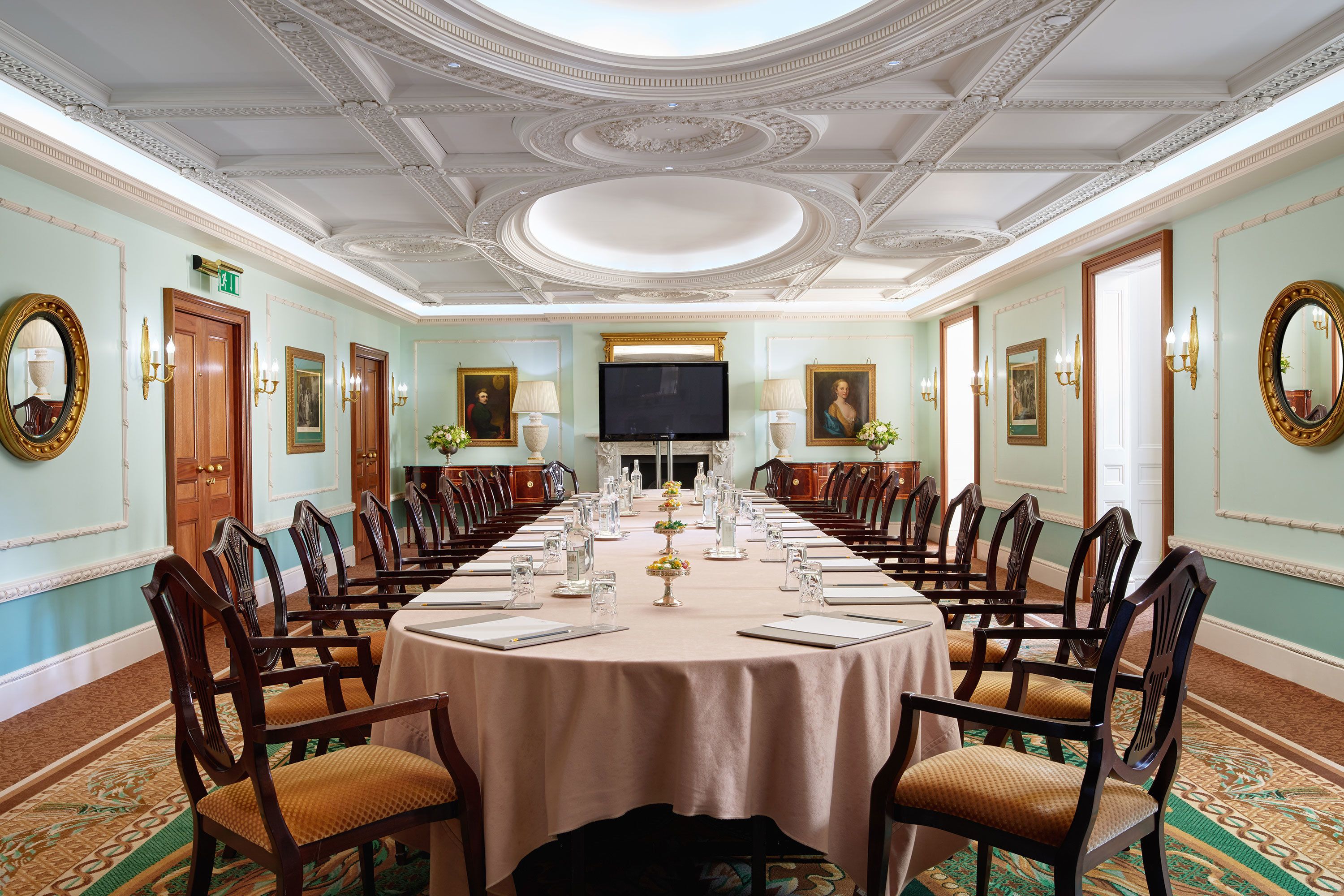 Uma sala de reuniões formal com uma mesa comprida, cadeiras e uma tela de televisão.
