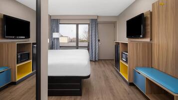 Quarto de hotel com cama, duas televisões, escrivaninha e vista para o exterior.