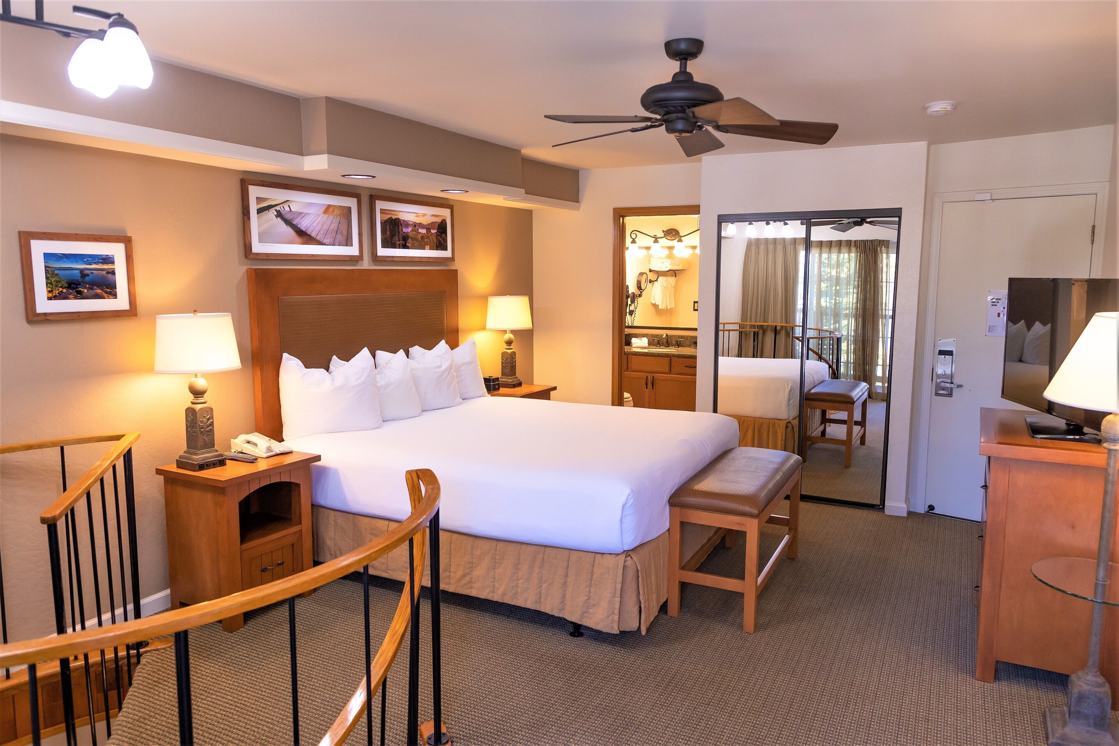 Quarto de hotel com cama grande, cabeceira de madeira, luminárias de apoio, escrivaninha e espelho.