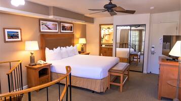 Quarto de hotel com cama grande, cabeceira de madeira, luminárias de apoio, escrivaninha e espelho.