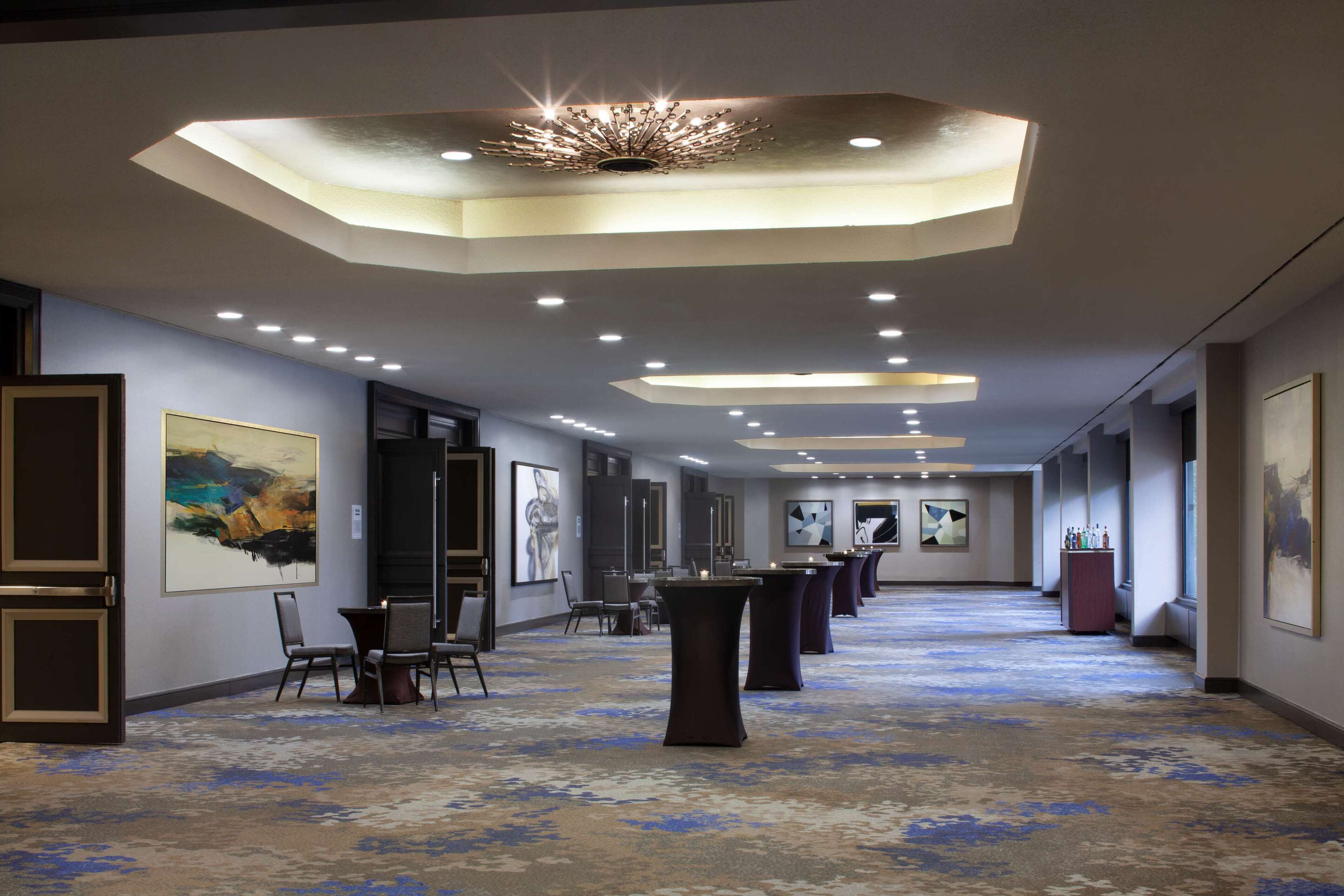 Corredor de hotel com iluminação embutida, design de teto diferenciado e obras de arte nas paredes.