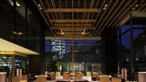 Uma área de estar moderna, com mesas e sofás, e grandes janelas que oferecem vista para o horizonte urbano à noite.