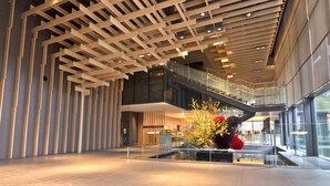 Um hall amplo com design de teto moderno, escadaria de vidro e arranjo floral central.