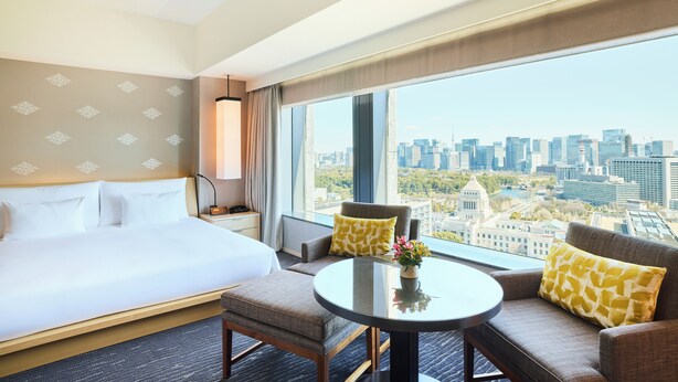 Quarto de hotel com uma cama grande, um sofá, uma mesa pequena e vista para a cidade.