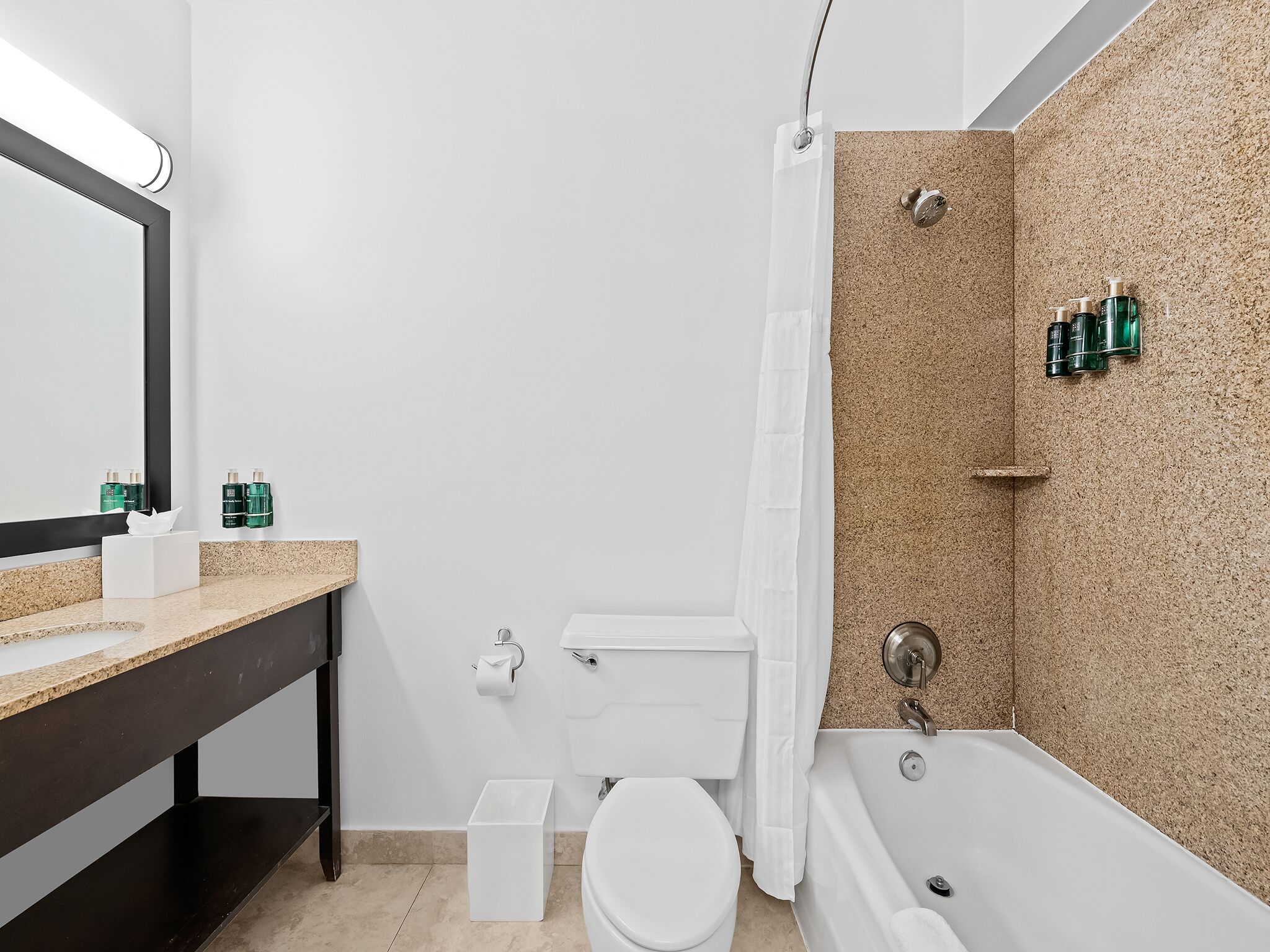 Uma casa de banho moderna com sanita, lavatório e banheira. Há produtos de higiene no balcão e um porta-toalhas.