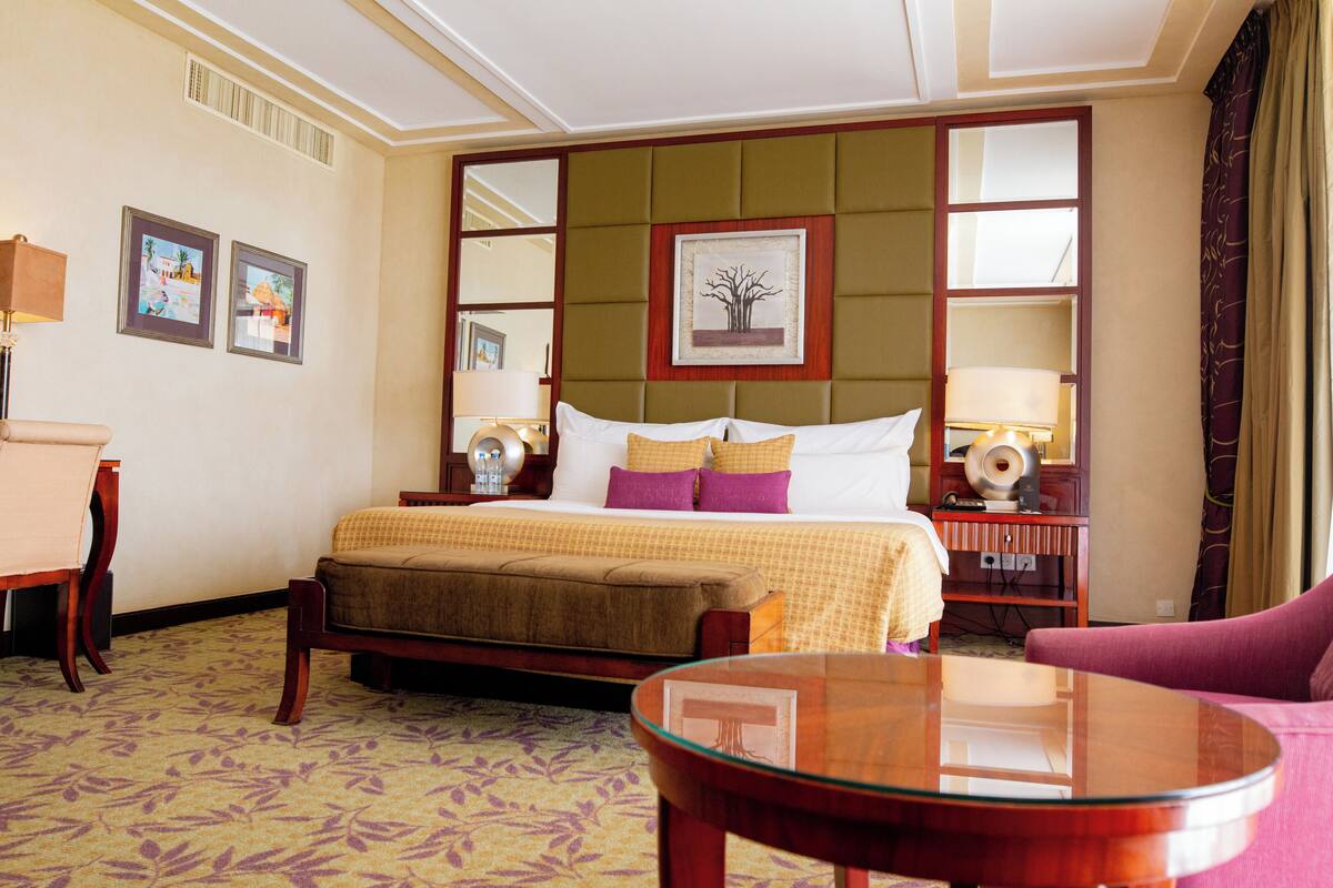 Quarto de hotel com cama, mesa de centro de vidro, sofá, escrivaninha e uma cadeira.