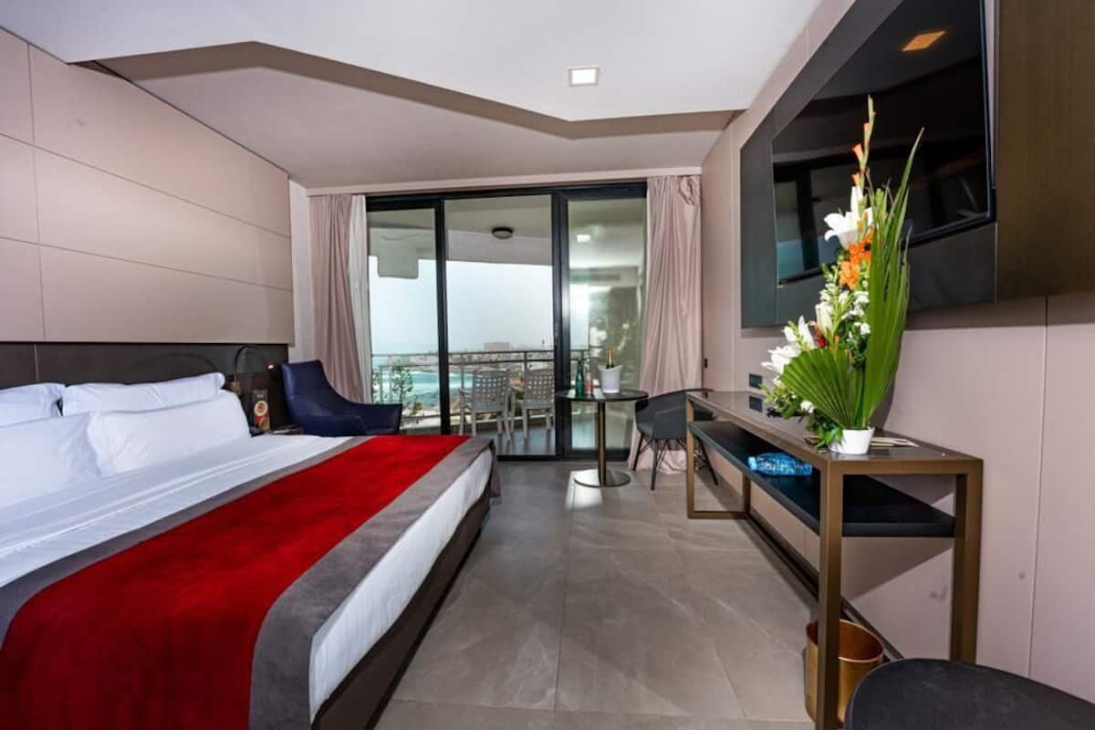 Quarto de hotel moderno com uma cama grande, uma mesa, uma cadeira e uma varanda com vista.