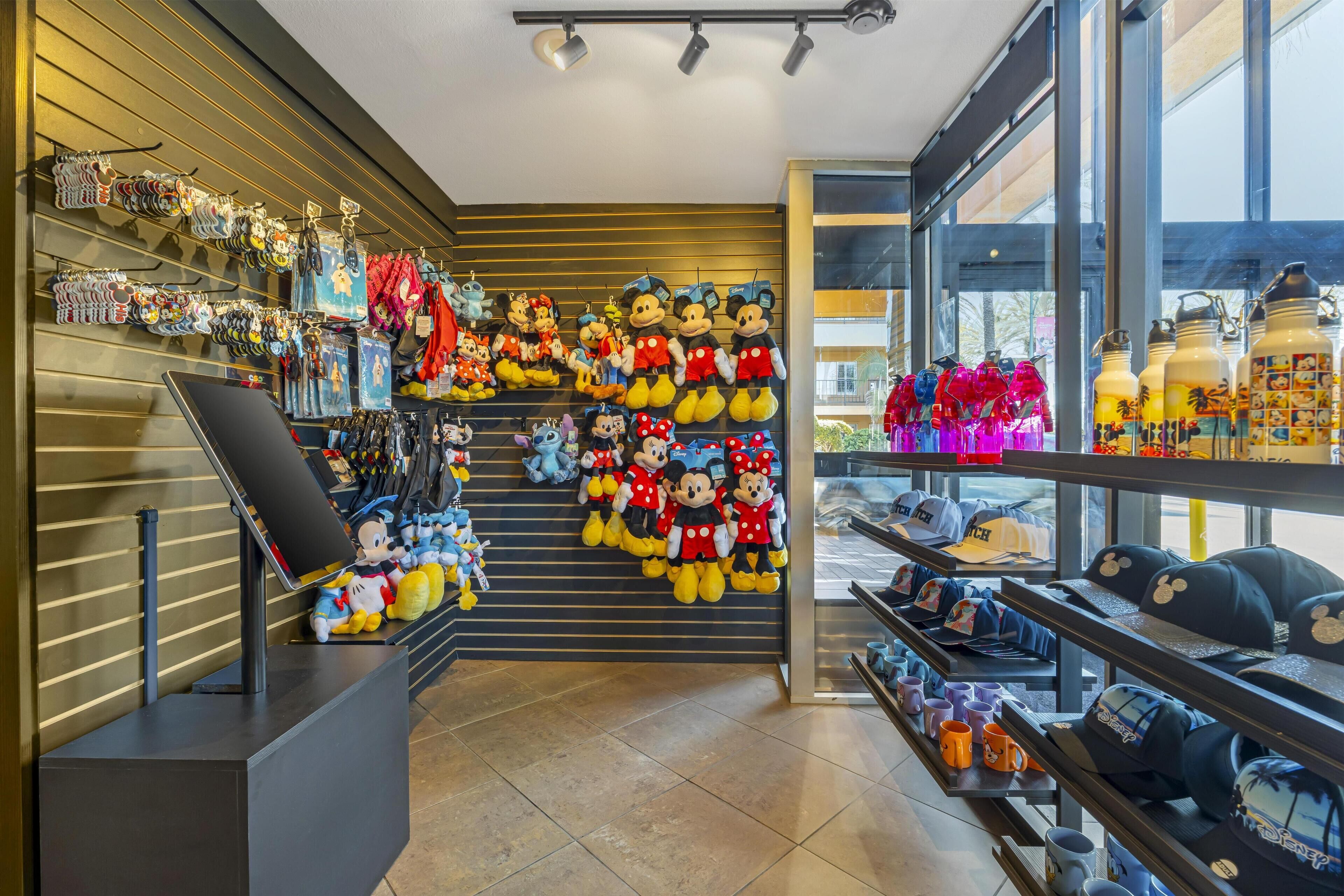 Uma loja com prateleiras cheias de brinquedos de pelúcia e chapéus do Mickey Mouse.