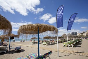 Praia com cadeiras de praia, guarda-sóis e bandeiras indicando um clube de praia.