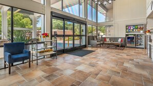 Ampla sala de estar com grandes janelas, vista para a piscina e cozinha moderna com frigorífico e prateleiras.