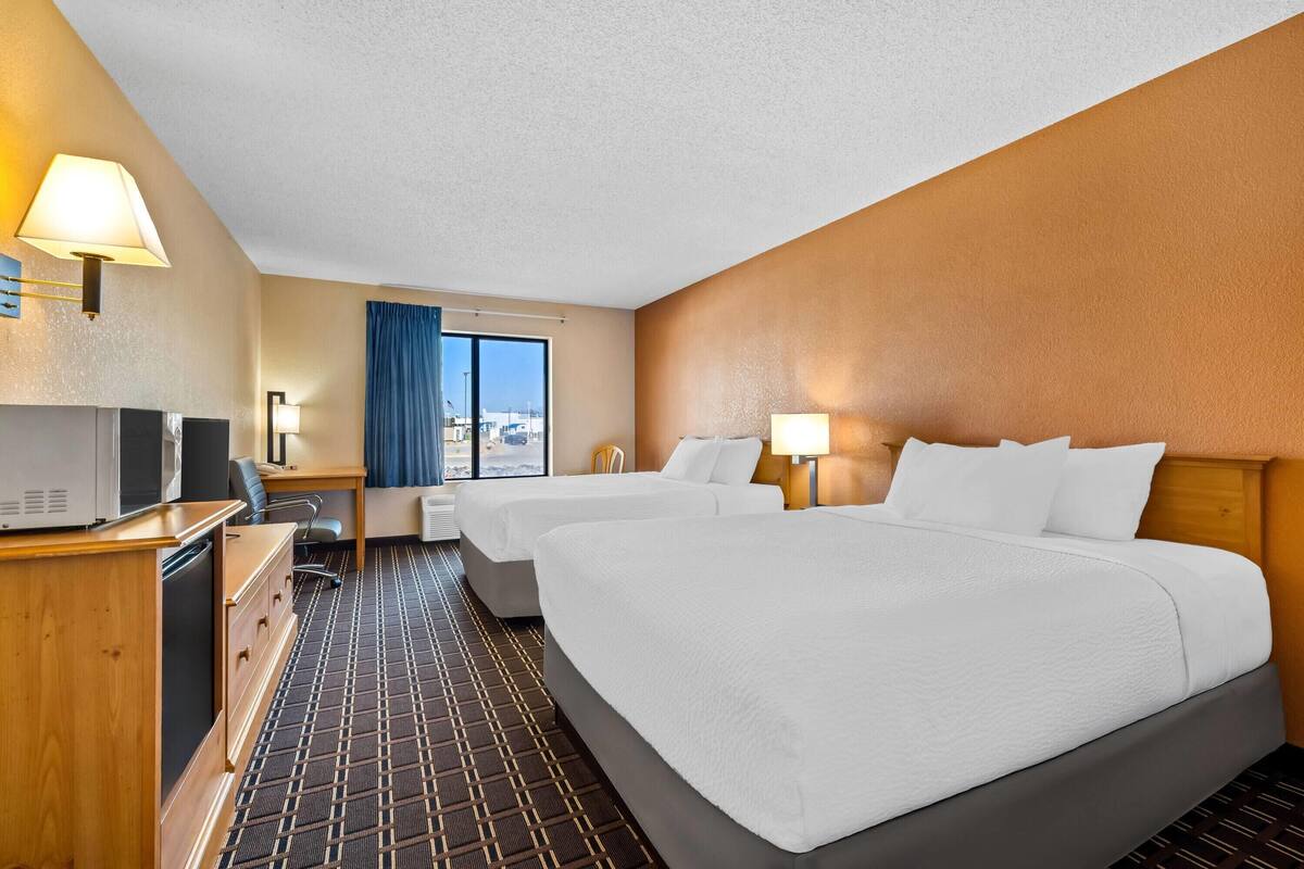 Quarto de hotel com duas camas, uma escrivaninha com computador, uma cadeira e uma janela com vista.