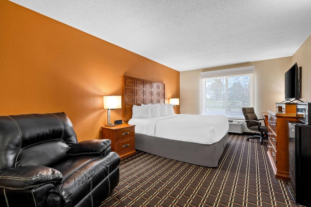 Quarto de hotel com cama, escrivaninha, cadeira, televisão e janela.