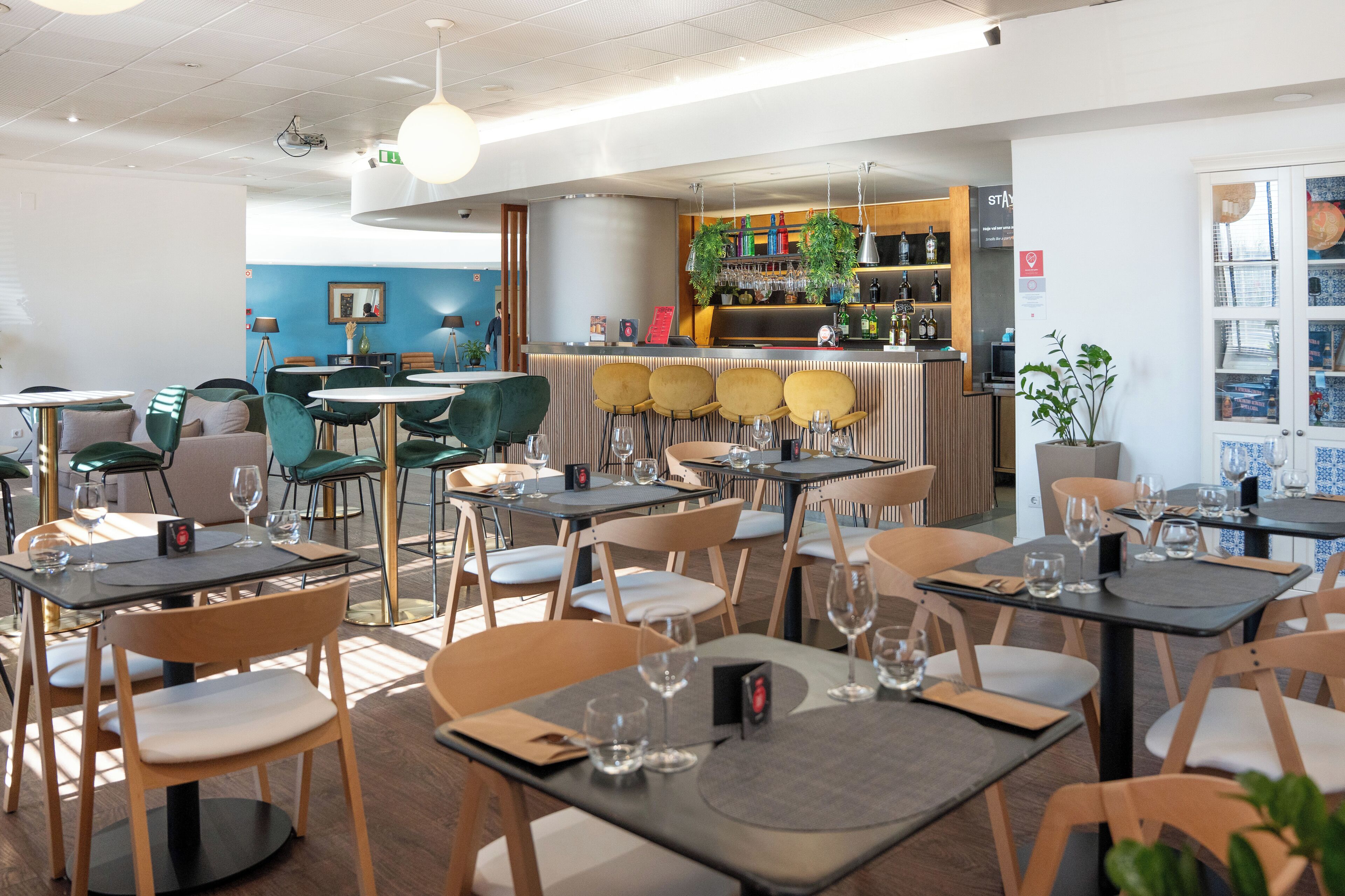 Interior de restaurante com mesas redondas, cadeiras e um espaço de bar.