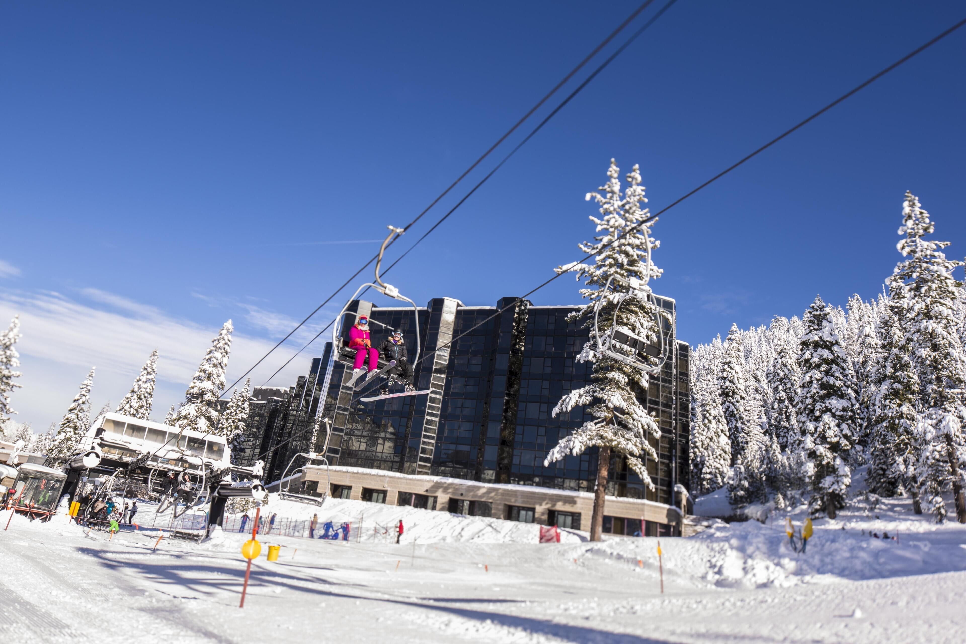 Estância de esqui com teleférico, árvores cobertas de neve e um edifício com uma pista de esqui em primeiro plano.
