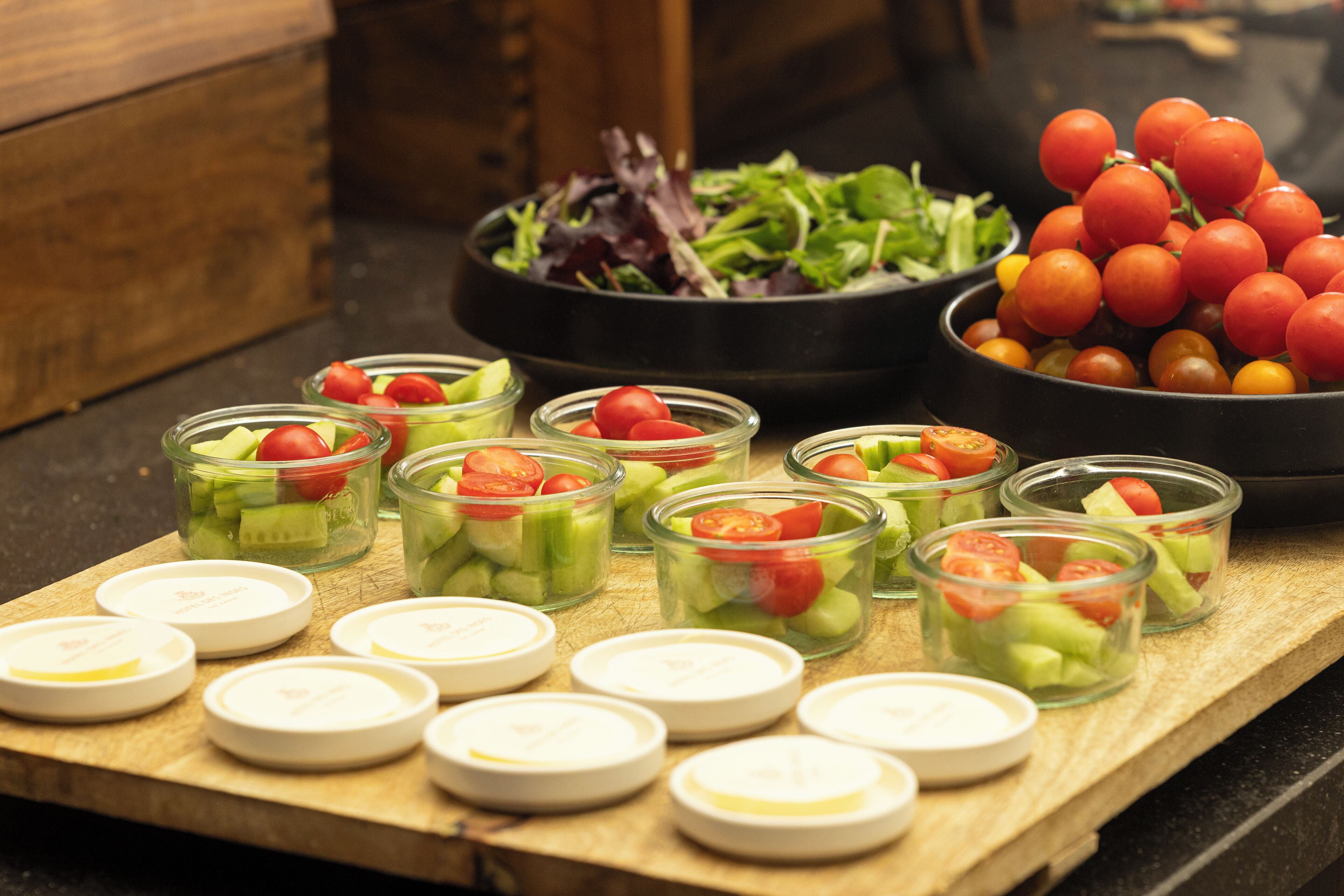 Uma tábua de madeira com vários recipientes de vidro contendo salada e pequenos potes de molho.