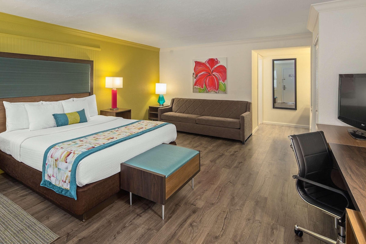 Quarto de hotel com cama, sofá, escrivaninha e televisão.