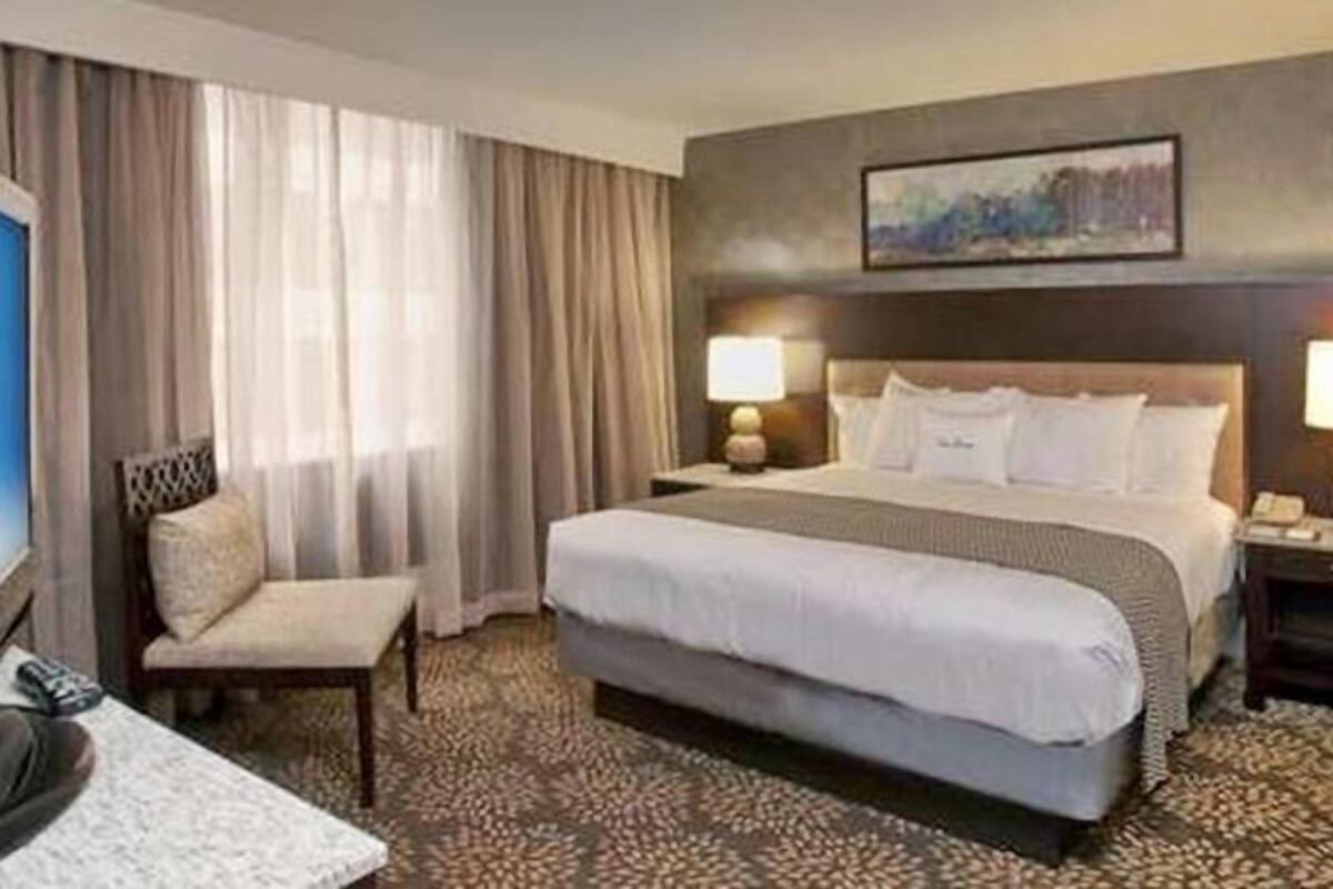 Quarto de hotel com cama, poltrona, escrivaninha, abajur e um quadro na parede.