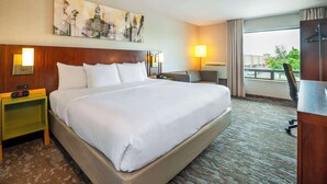 Quarto de hotel com uma cama grande, uma escrivaninha, uma cadeira e vista para o exterior.