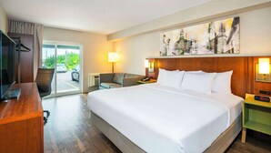 Quarto de hotel com uma cama grande, escrivaninha, cadeira, televisão, um quadro na parede e vista para o exterior.