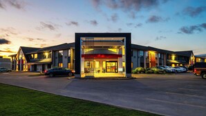 Um hotel moderno com entrada central, vários lugares de estacionamento e um jardim bem cuidado.