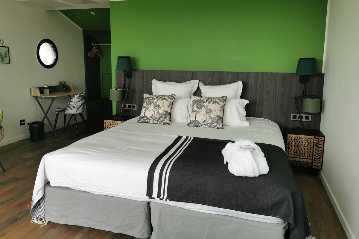 Quarto de hotel moderno com uma cama grande, uma escrivaninha e uma parede verde de destaque.