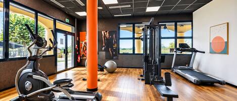 Academia com máquinas de cardio, pesos livres e um grande pilar laranja.