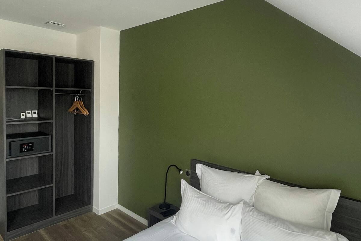 Quarto com cama, mesa de cabeceira, guarda-roupa e parede verde.