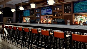 Uma área de bar com várias televisões exibindo esportes, um bar bem abastecido e banquetas acolchoadas cor de laranja.