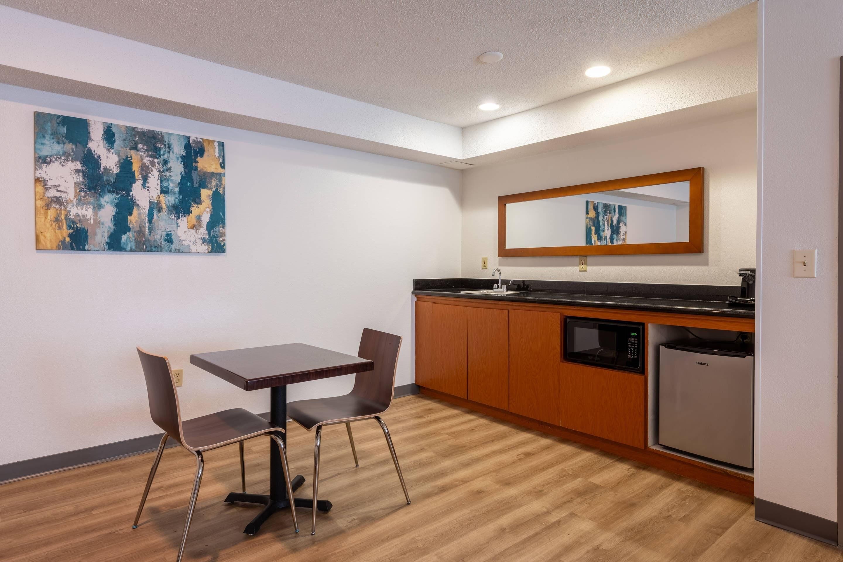 Uma cozinha compacta com área de refeições, piso de madeira e um quadro abstrato grande na parede.