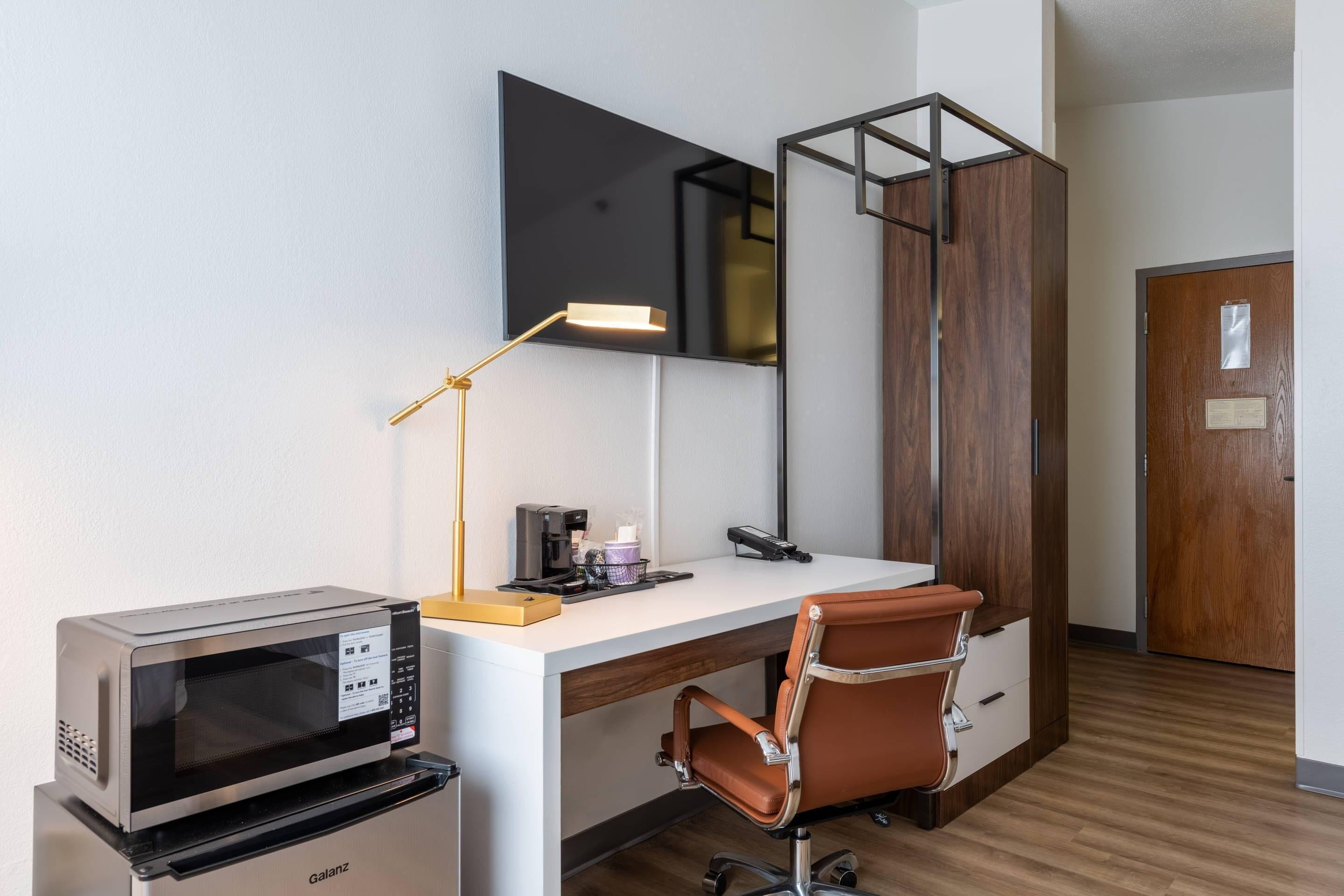 Quarto de hotel com cozinha compacta, uma mesa com cadeira, luminária de mesa, micro-ondas e um espelho grande.