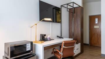 Quarto de hotel com cozinha compacta, uma mesa com cadeira, luminária de mesa, micro-ondas e um espelho grande.