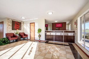 Uma área de recepção de hotel, com balcão de check-in, mesa de atendimento e espaço com vista.