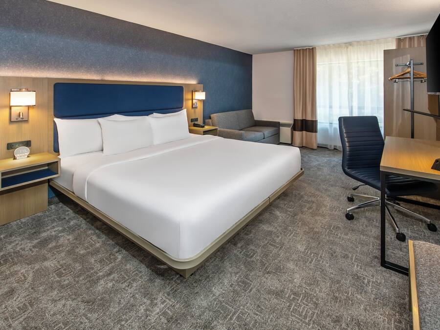Quarto de hotel com uma cama grande, uma escrivaninha com cadeira, televisão e janela com cortinas.