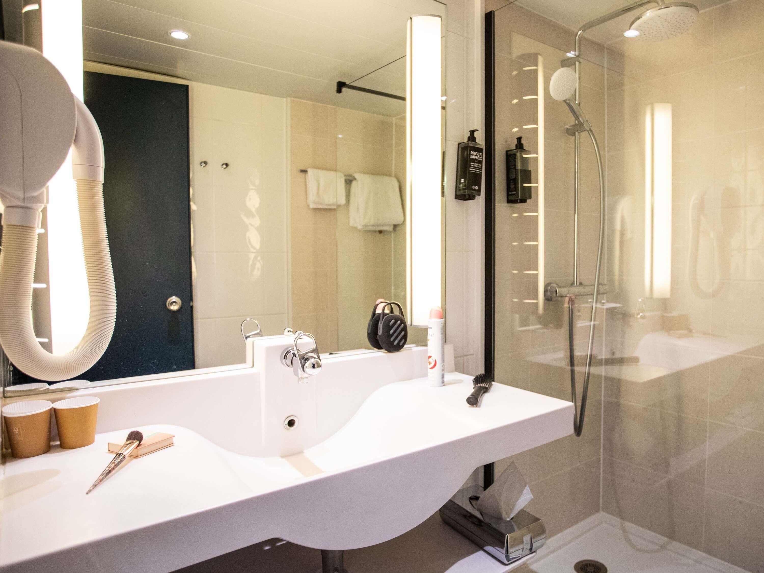 Uma casa de banho moderna com um espelho grande, duas pias, um secador de cabelo e uma cabine de duche em vidro.