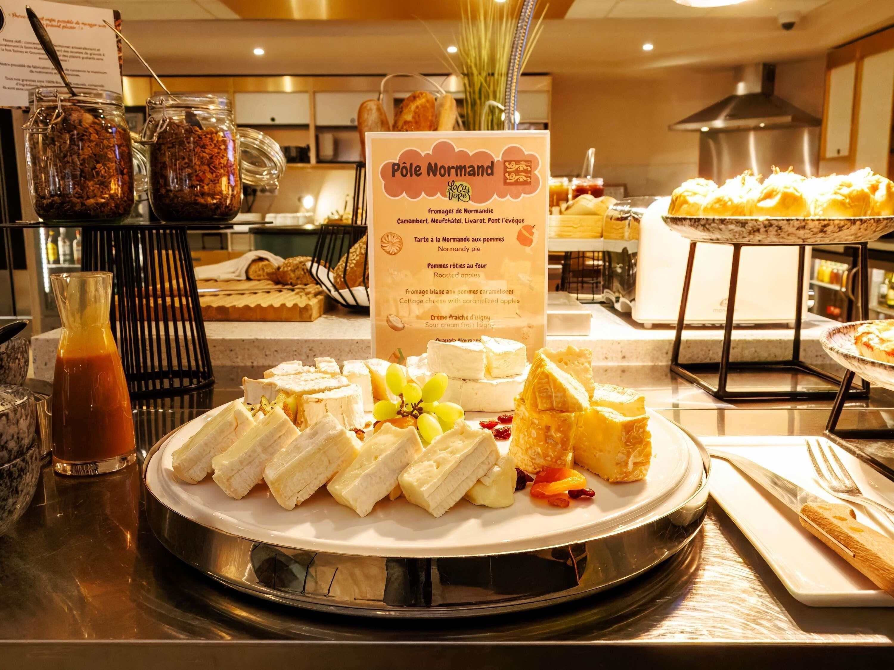 Buffet com variedade de queijos, frutas e uma placa indicando o cardápio.