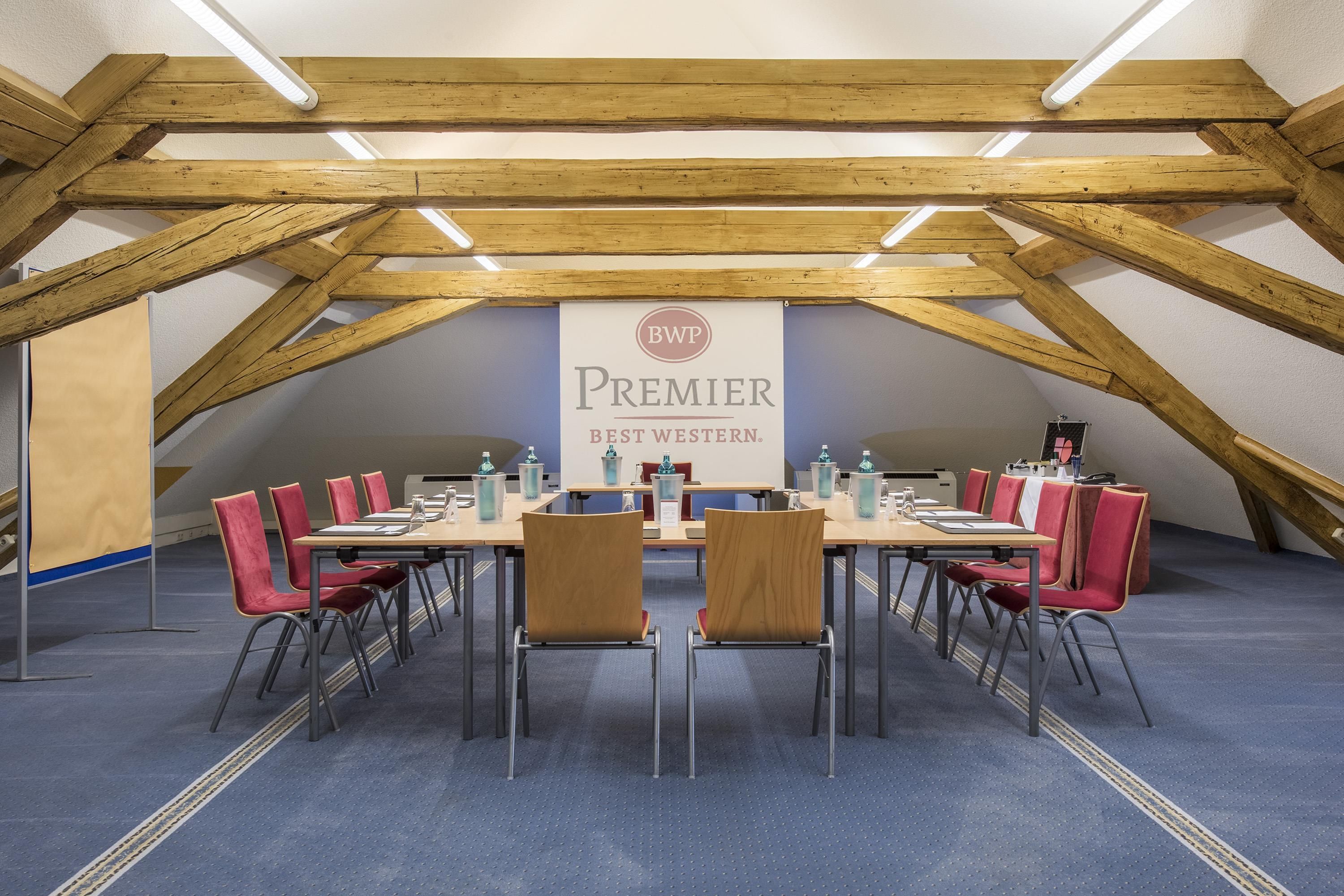 Uma sala de conferências com uma mesa comprida, cadeiras vermelhas e um banner com a inscrição 'Premier Best Western'.